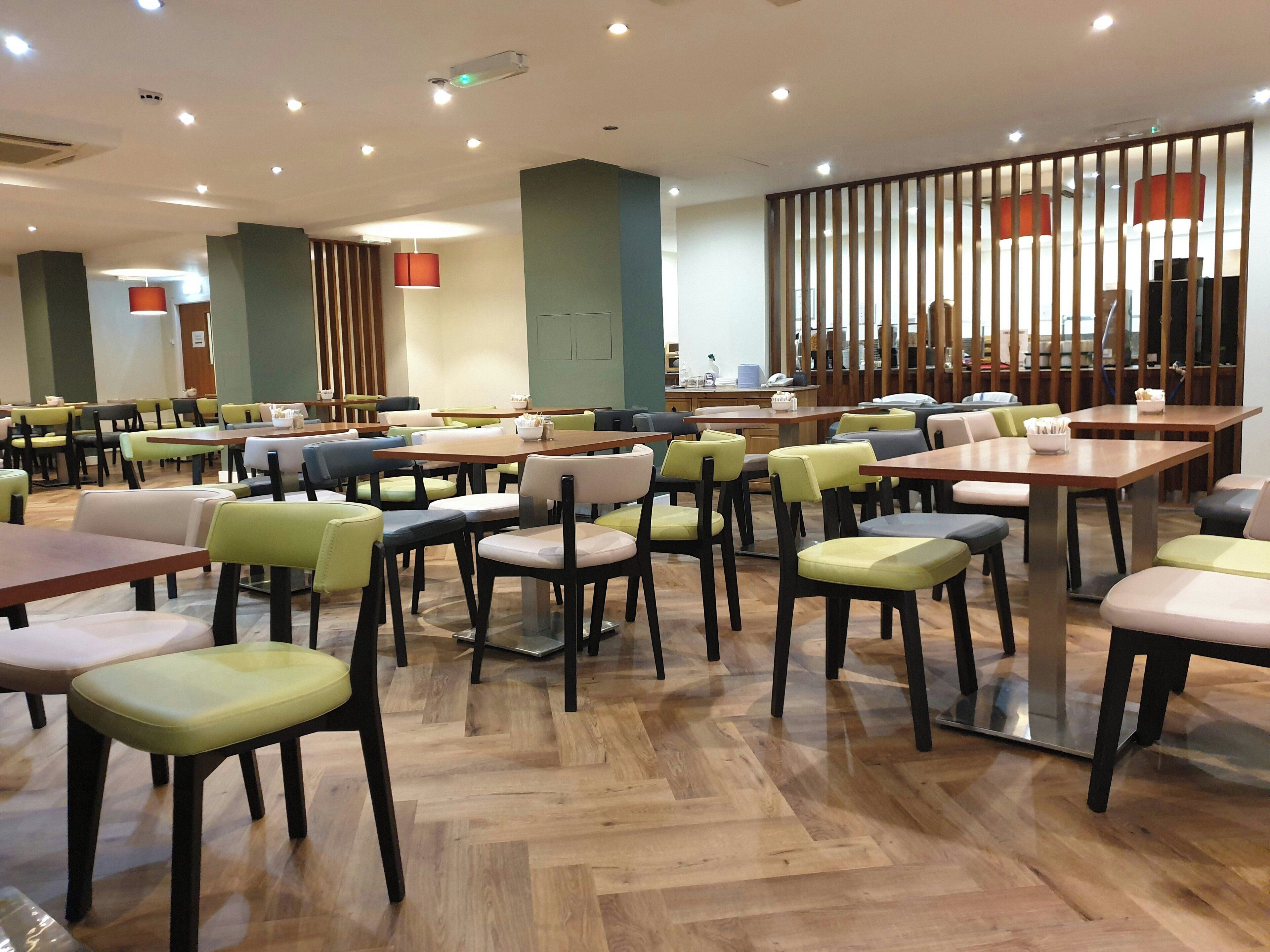 Uma sala de jantar espaçosa com várias mesas e cadeiras, piso de madeira e um design de teto moderno.