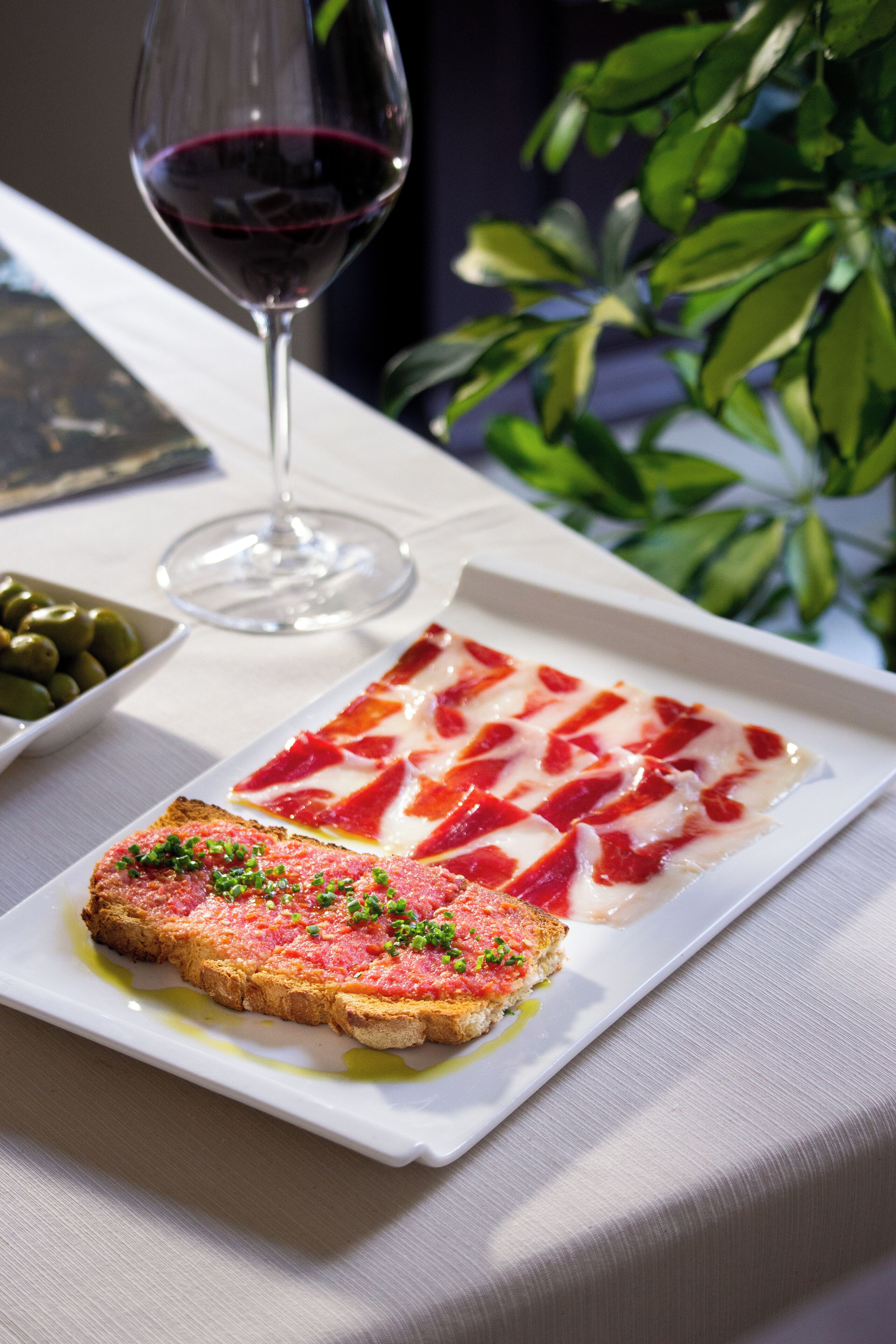 Prato de comida com um copo de vinho tinto e um recipiente de azeitonas.