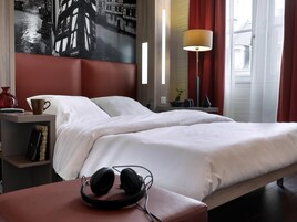 Quarto de hotel com cama, mesa de cabeceira, abajur e um quadro pendurado na parede.