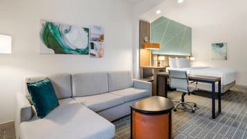 Quarto de hotel moderno com sofá, mesa redonda, cama e escrivaninha.
