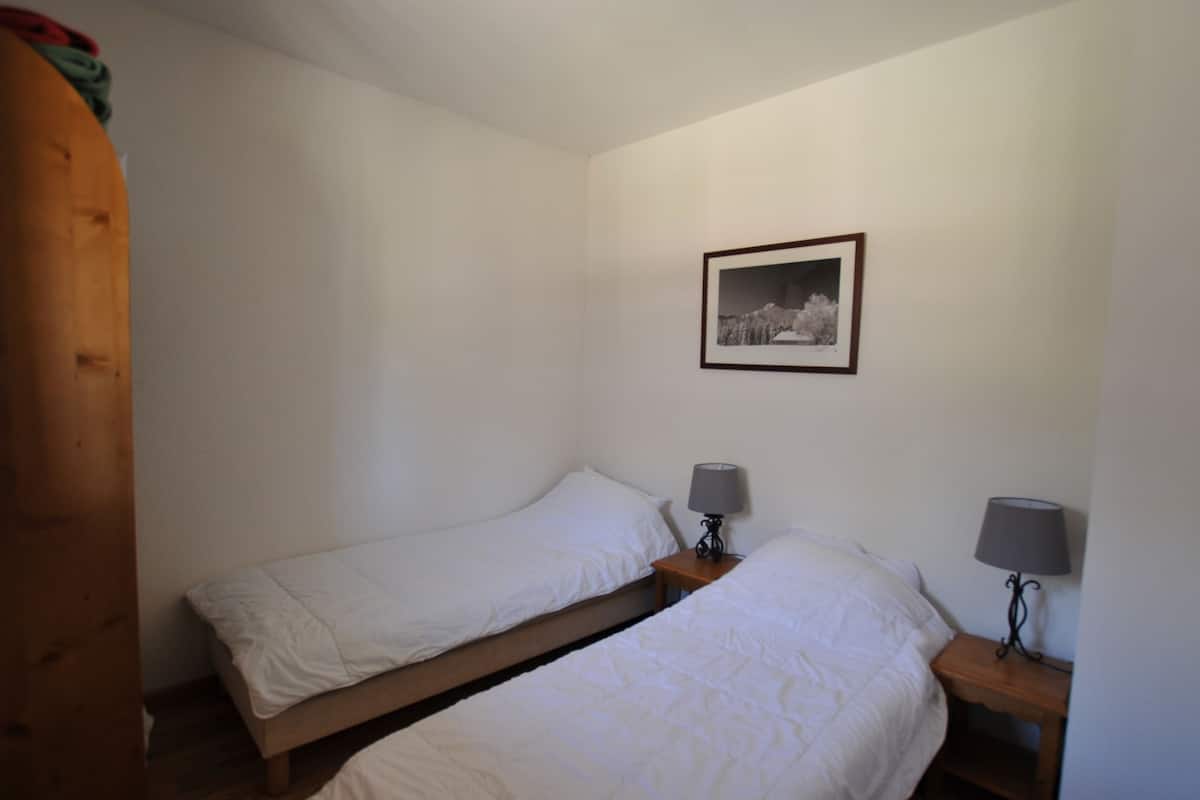 Um quarto pequeno e simples com duas camas de solteiro, cabeceiras de madeira e abajures.