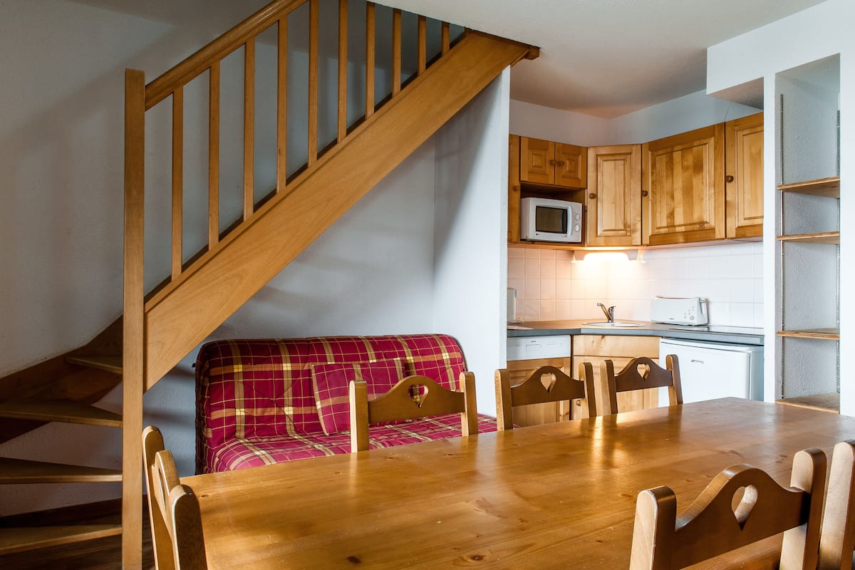 Escada de madeira leva a um quarto no mezanino com um sofá de retalhos vermelhos.