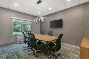 Sala de conferência com uma mesa grande, quatro cadeiras, uma TV de tela plana e janela com vista para vegetação.