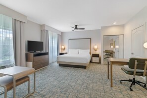 Quarto de hotel com cama, escrivaninha, cadeira, televisão e ventilador de teto.