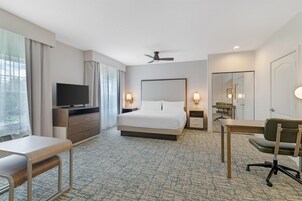 Quarto de hotel com cama, escrivaninha, cadeira, televisão e ventilador de teto.