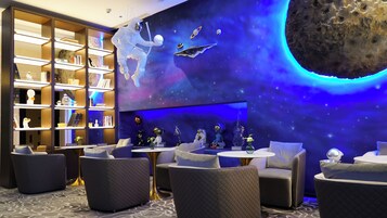 Quarto com mural temático do espaço, estante de livros e área de estar.