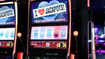 Duas máquinas caça-níqueis com letreiros iluminados que dizem "I ♥ JACKPOTS!" e "Colecione corações para ganhar jackpots!"