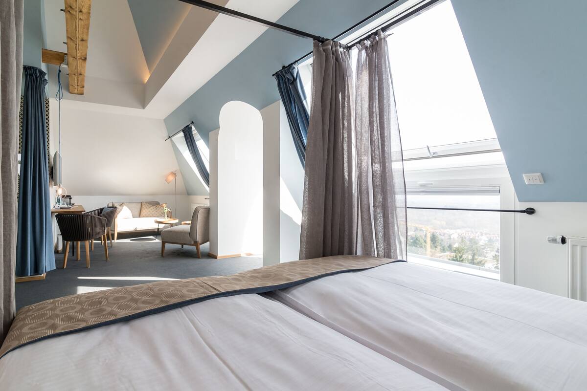 Quarto de hotel moderno com uma cama grande, uma escrivaninha e uma cadeira. Há vista para a cidade pela janela.