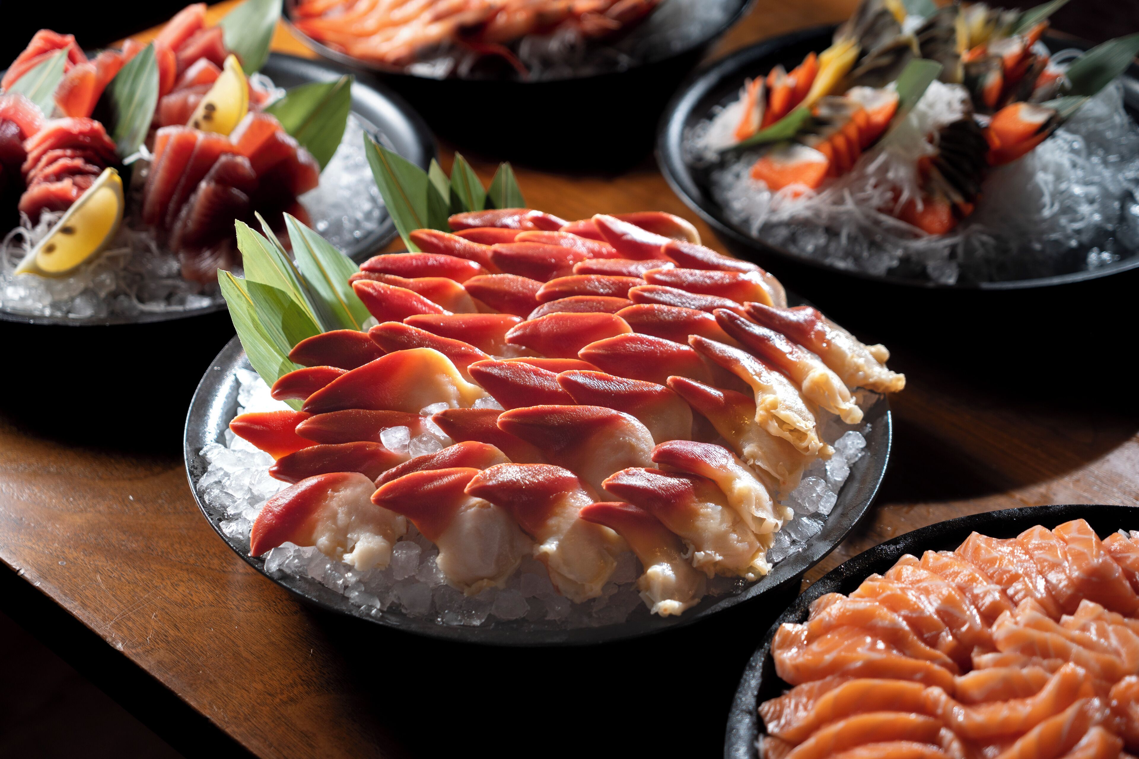Diversos pratos de sushi sobre gelo, incluindo fatias de salmão e atum, decorados com folhas verdes.