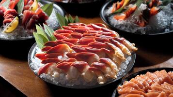 Diversos pratos de sushi sobre gelo, incluindo fatias de salmão e atum, decorados com folhas verdes.