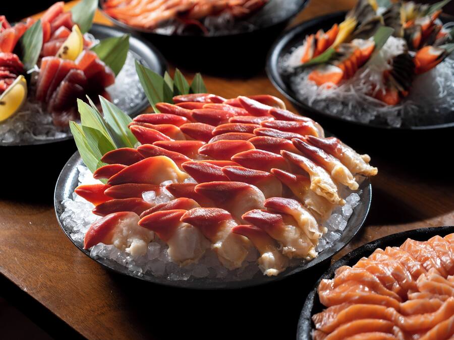 Diversos pratos de sushi sobre gelo, incluindo fatias de salmão e atum, decorados com folhas verdes.