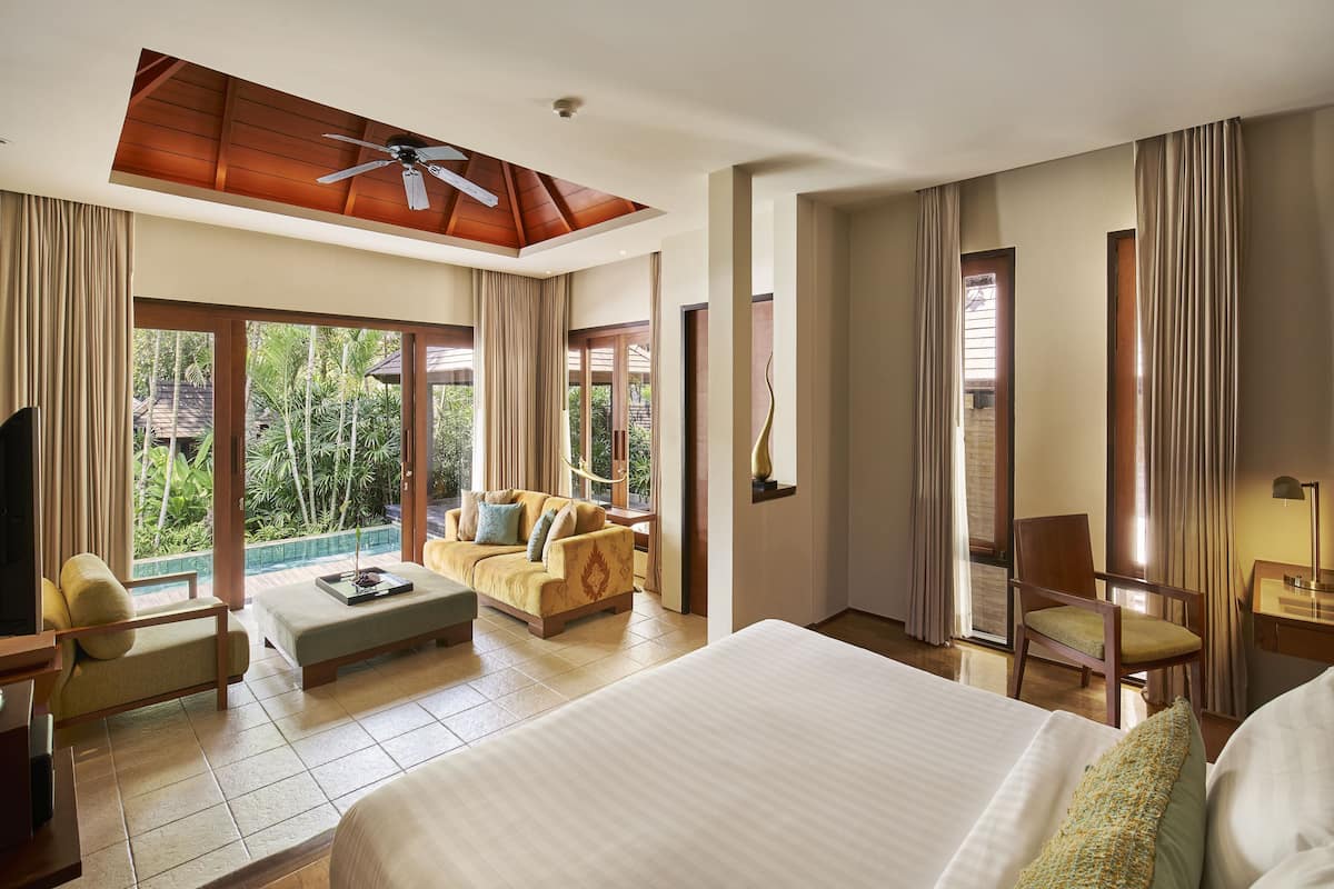 Quarto de hotel espaçoso com uma cama grande, sofá, poltrona e escrivaninha. Possui varanda com vista para o verde.