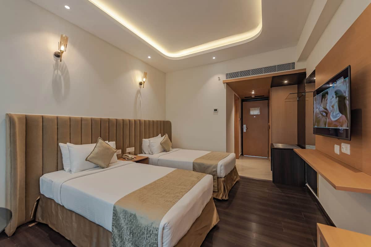 Quarto de hotel com duas camas, televisão e escrivaninha.