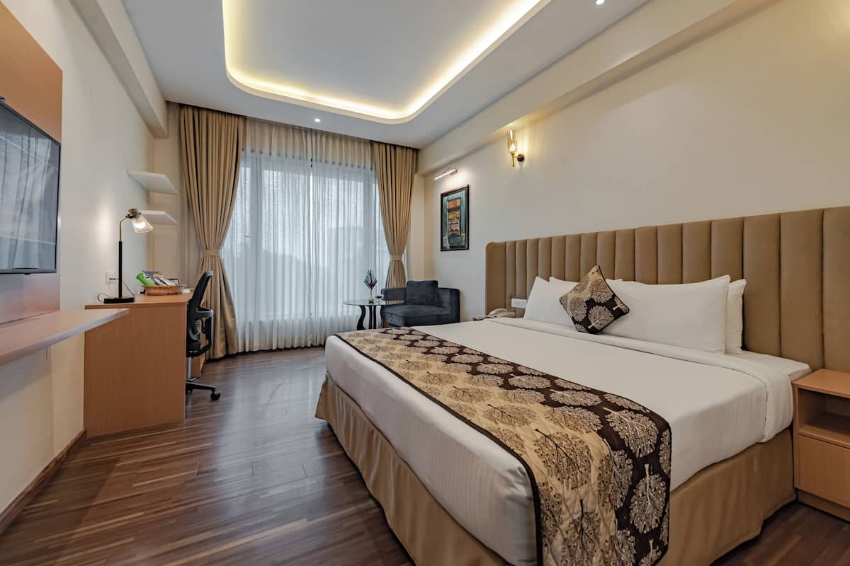 Quarto de hotel com uma cama grande, uma escrivaninha, uma cadeira, uma televisão e uma janela com cortinas.