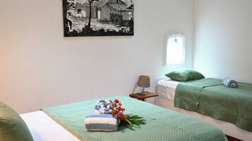 Quarto com duas camas, um quadro na parede, uma janela e uma mesa de cabeceira com abajur.