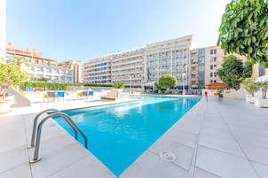 Piscina com escada de metal, rodeada por um deck ladrilhado e mobiliário para área externa.