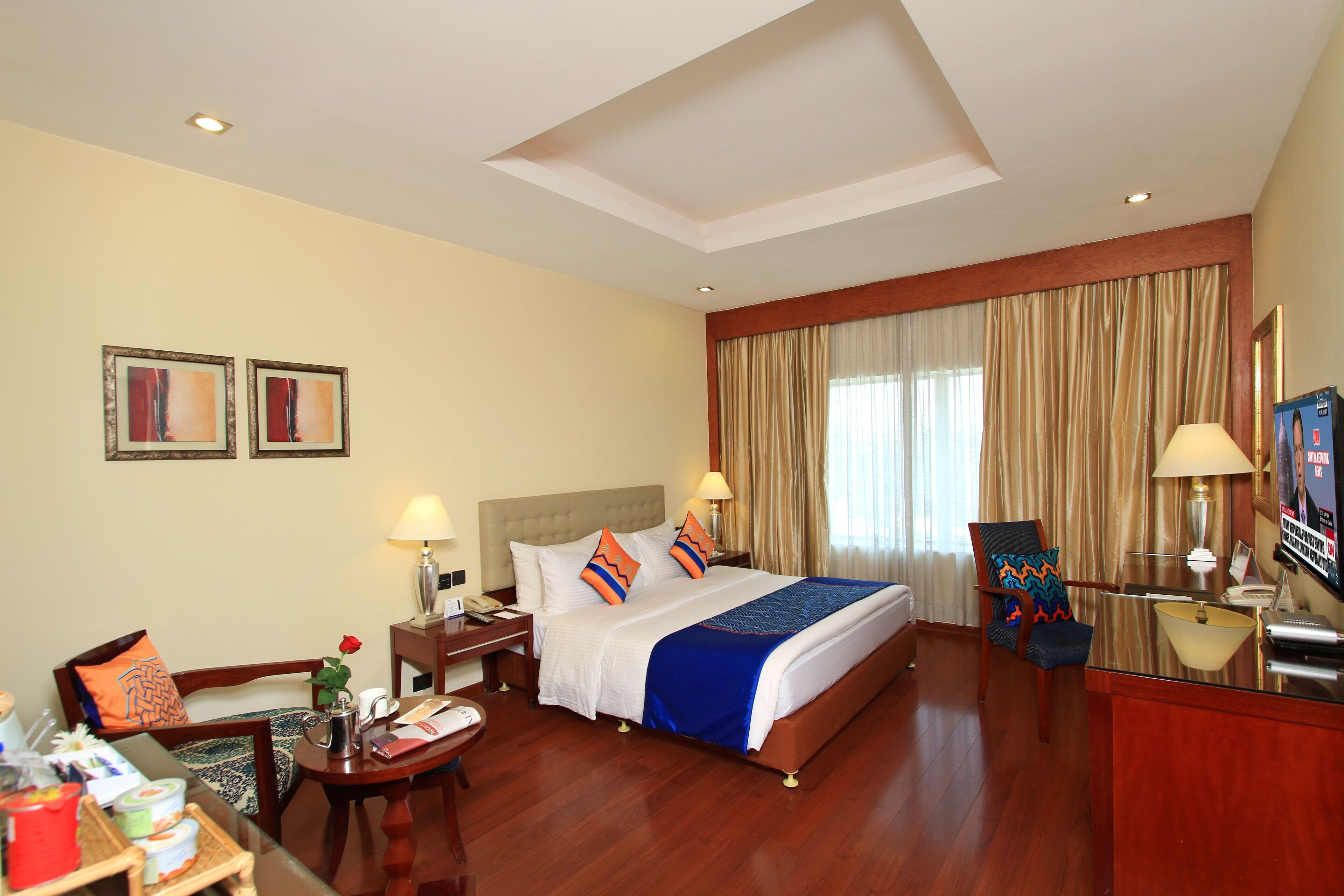 Quarto de hotel com uma cama grande, duas mesas de cabeceira, uma escrivaninha, uma cadeira e uma televisão.