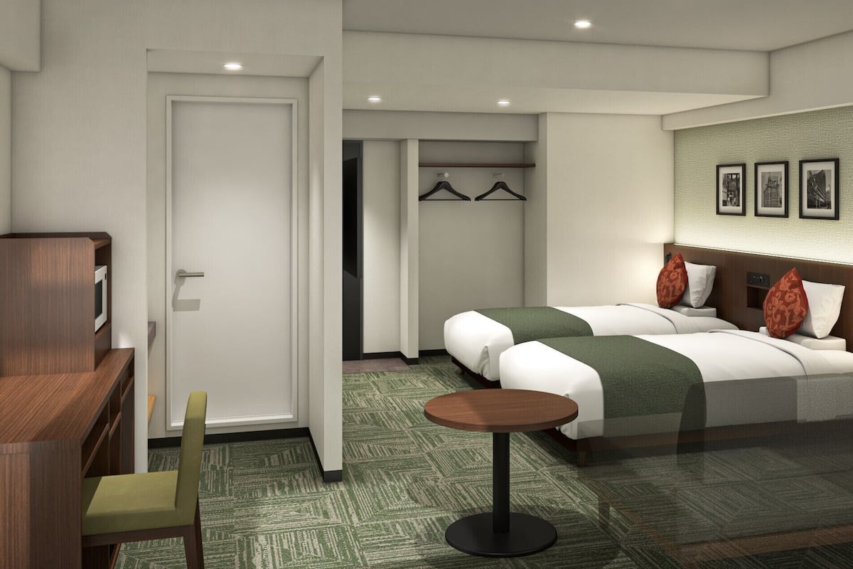 Quarto de hotel com cama, uma cadeira, uma mesinha, guarda-roupa e cabideiro.