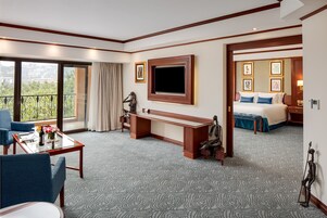 Quarto de hotel com uma cama grande, uma escrivaninha, uma televisão e uma varanda com cortinas.