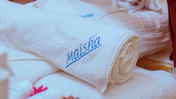 Toalha com a inscrição 'Malsha' bordada, enrolada sobre uma mesa.
