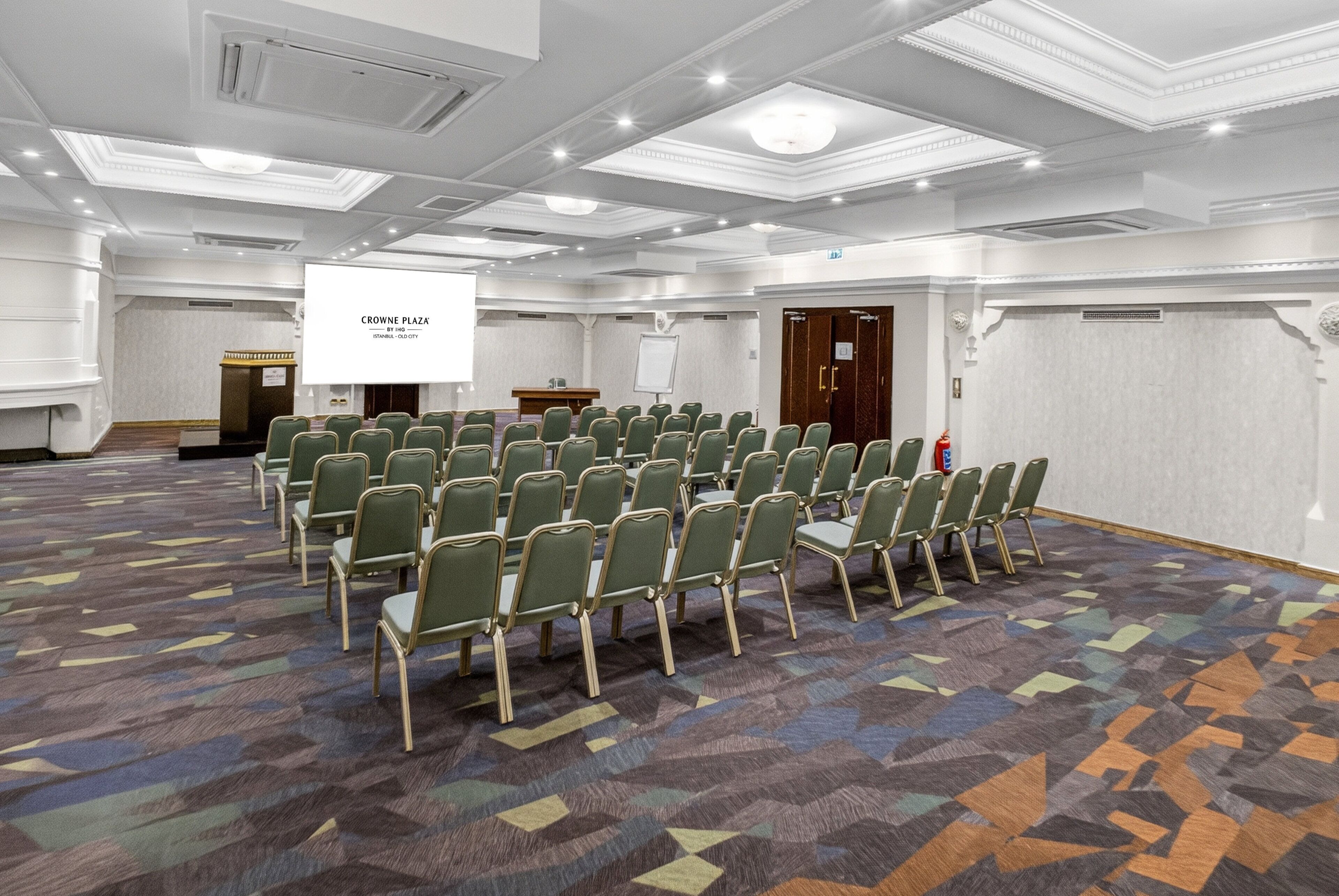 Uma sala de conferência com fileiras de cadeiras, um pódio e uma tela de projeção.