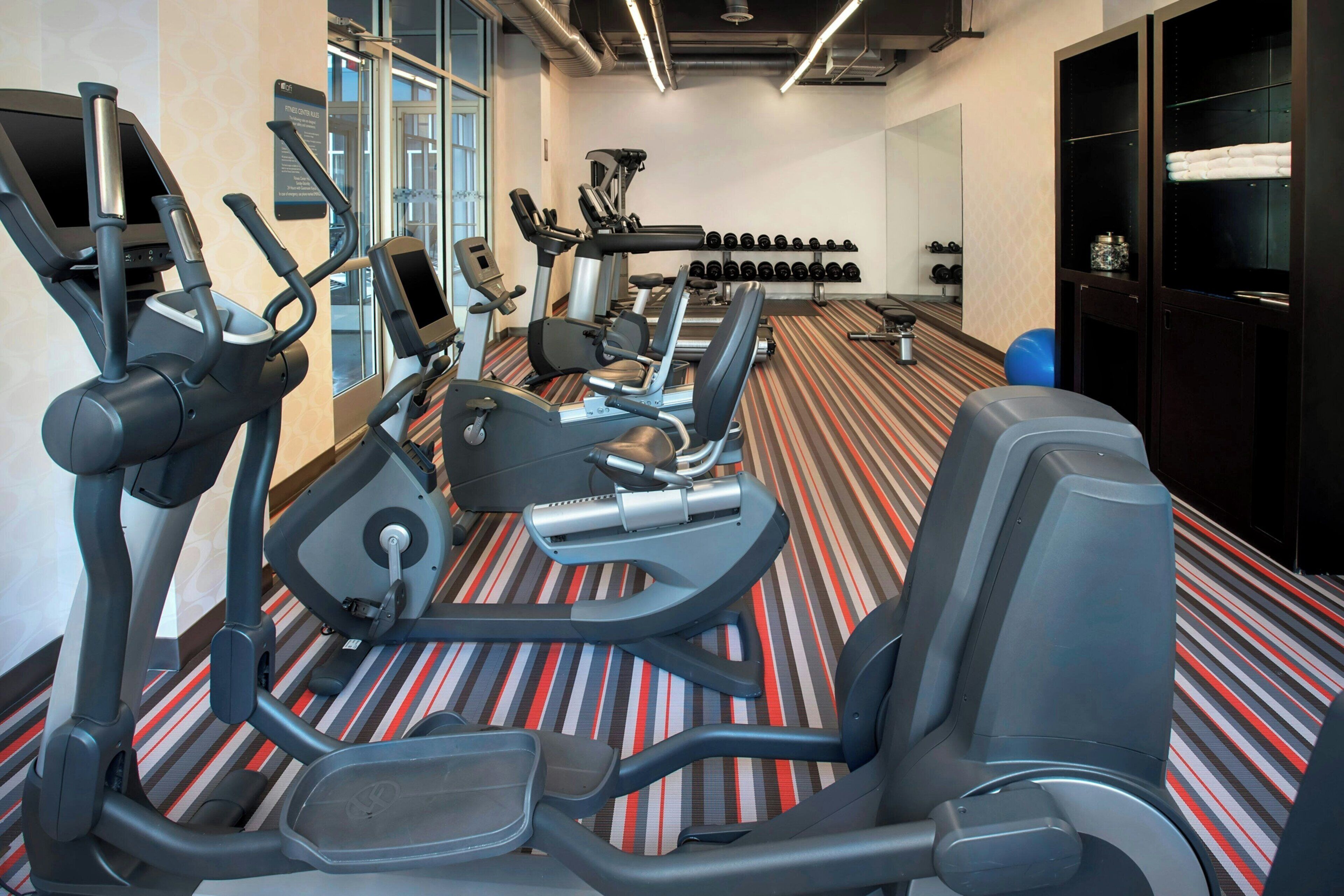 Uma academia com diversos equipamentos de ginástica, incluindo esteiras e halteres, e um tapete listrado.