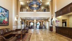 Um hall amplo com teto alto, um candelabro, assentos de couro, um balcão de recepção e uma grande pintura na parede.