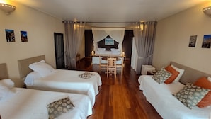 Quarto de hotel com duas camas, uma mesa de jantar e uma mesinha com um telefone.