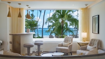 Uma sala de estar moderna com vista para o oceano, com espaço para bar, duas poltronas, uma mesa de centro redonda e iluminação pendente.