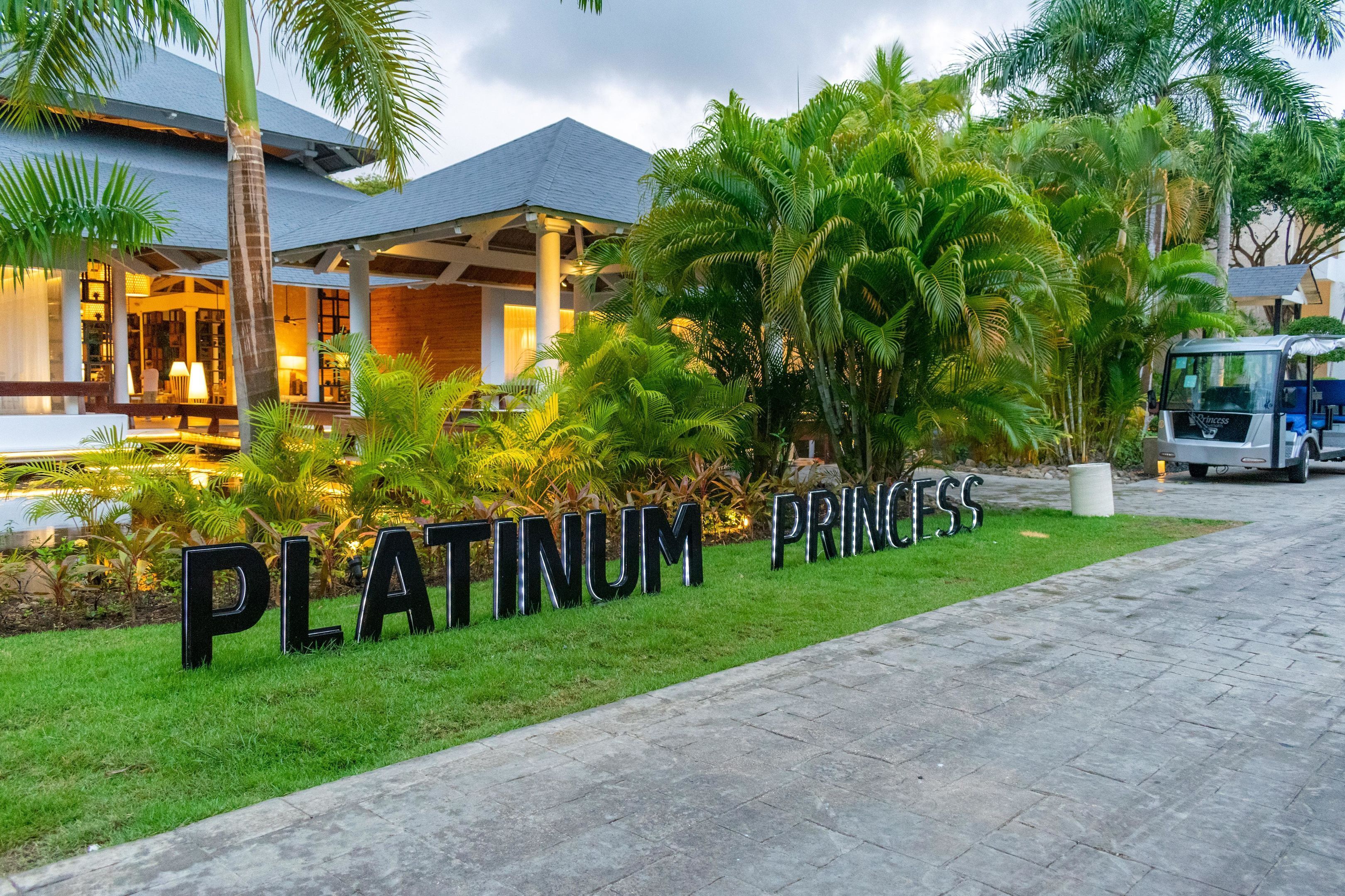 Entrada de hotel com uma placa indicando "PLATINUM PRINCESS" e um caminho pavimentado que leva ao edifício.