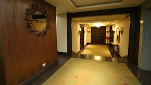 Corredor de hotel com parede de madeira, um espelho, chão coberto de carpete e uma porta no final.