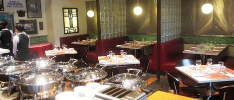 Disposição de buffet com várias estações de serviço, mesas e cadeiras em um restaurante.