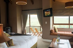 Quarto de hotel com cama, televisão, um assento junto à janela com vista e uma mesa com garrafas.