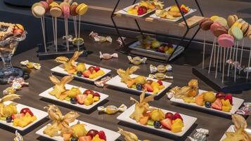 Mesa de buffet com diversos alimentos, incluindo frutas, doces e macarons.
