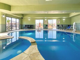 Piscina interna com água cristalina, prancha de mergulho e cadeiras de descanso.