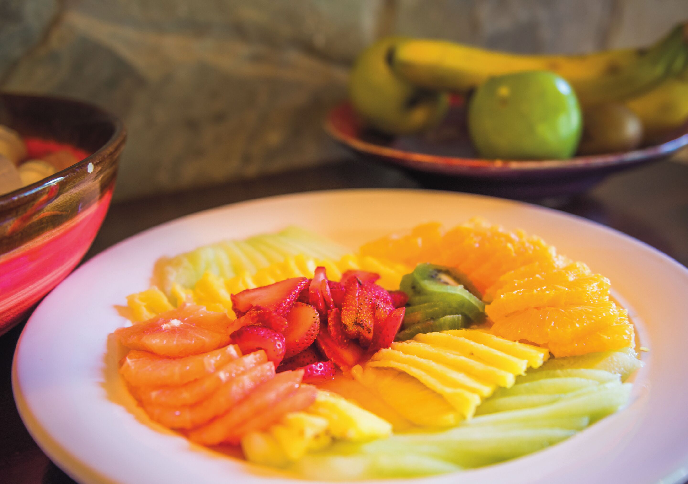Prato com fatias de frutas, incluindo manga, kiwi e morangos.