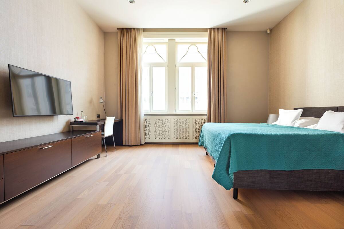Quarto de hotel moderno com cama, televisão, escrivaninha e janela com cortinas.