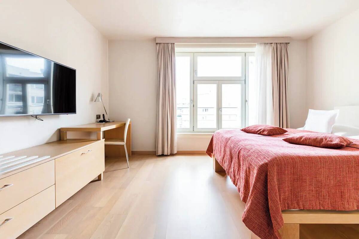 Quarto com cama, escrivaninha e televisão.