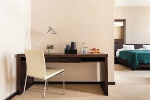 Quarto de hotel com escrivaninha, cadeira, abajur e cama com manta verde.