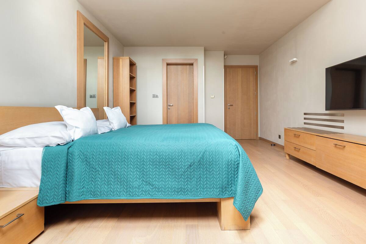 Quarto moderno com cama, guarda-roupa de madeira e televisão na parede.