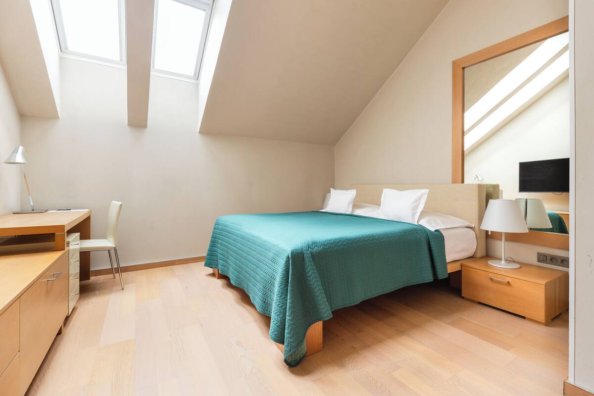 Quarto com cama, escrivaninha, cadeira e mesa de cabeceira com abajur.