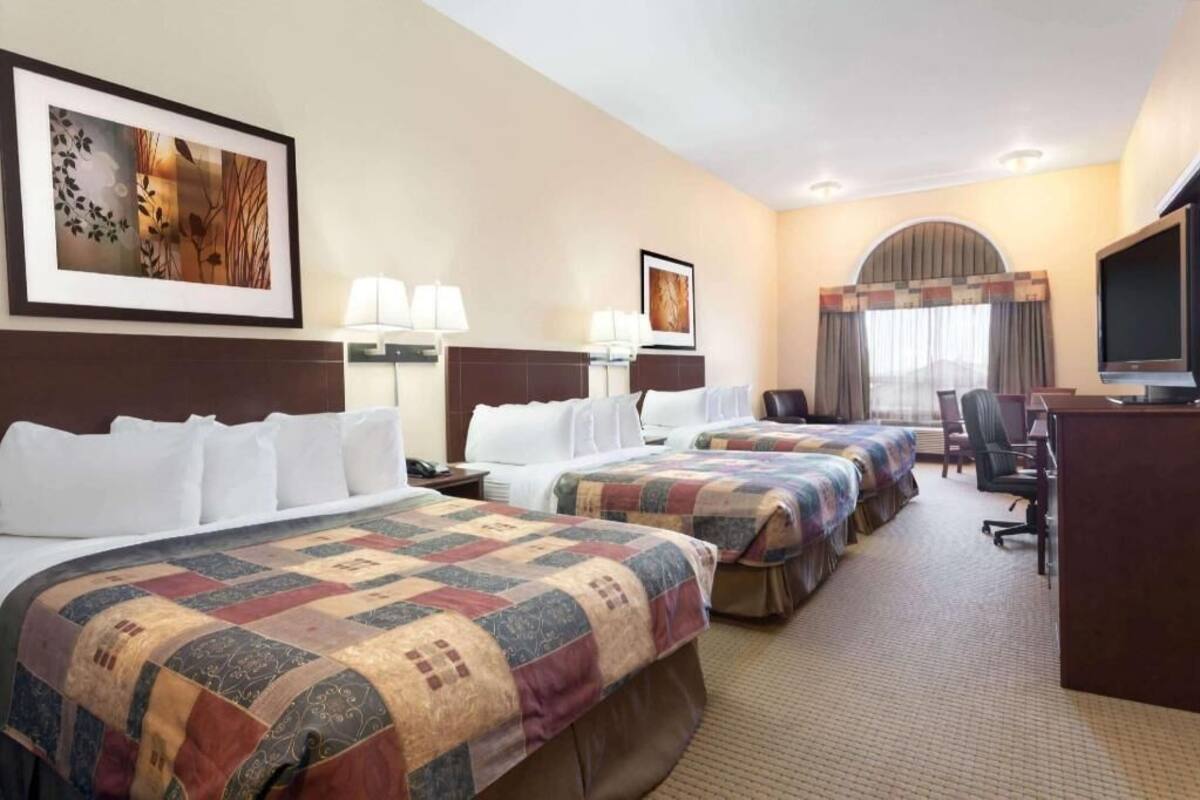Quarto de hotel com duas camas, uma mesa, uma televisão e uma janela grande.