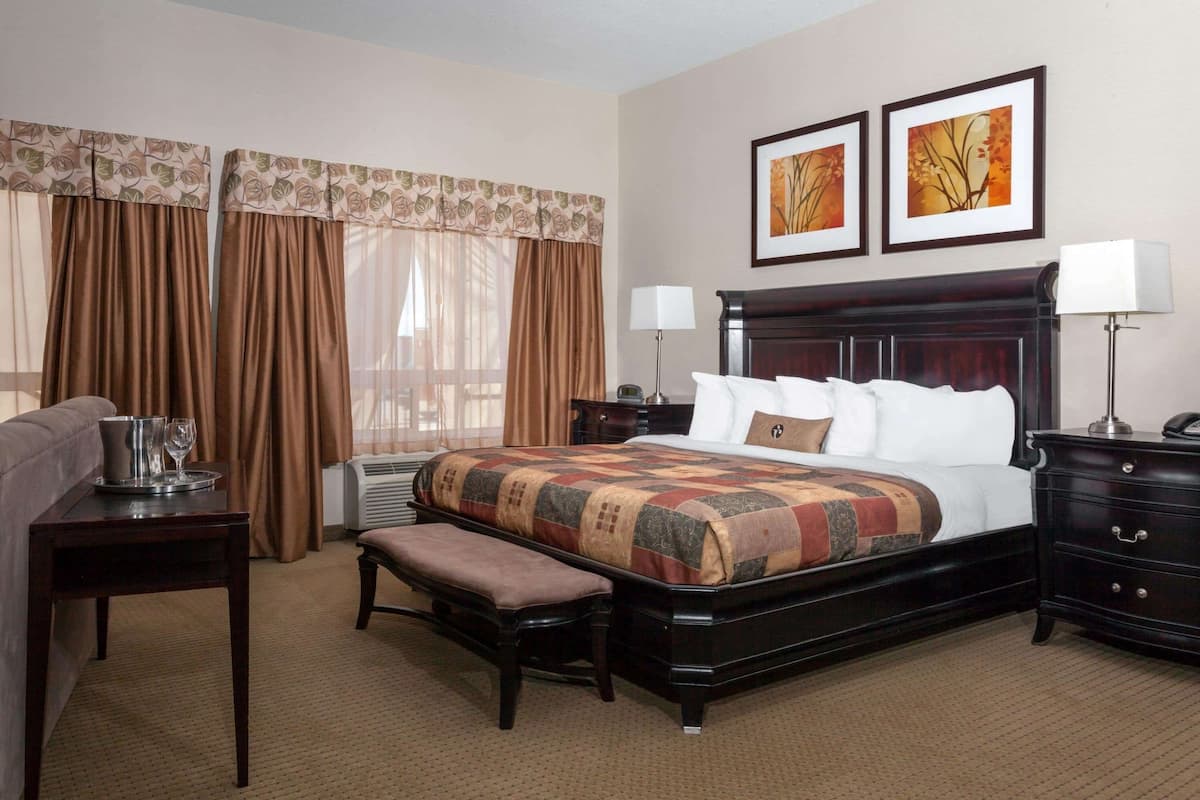 Quarto de hotel com uma cama grande, mesa de cabeceira com abajur, um banquinho, cômoda e ar-condicionado fixado na parede.