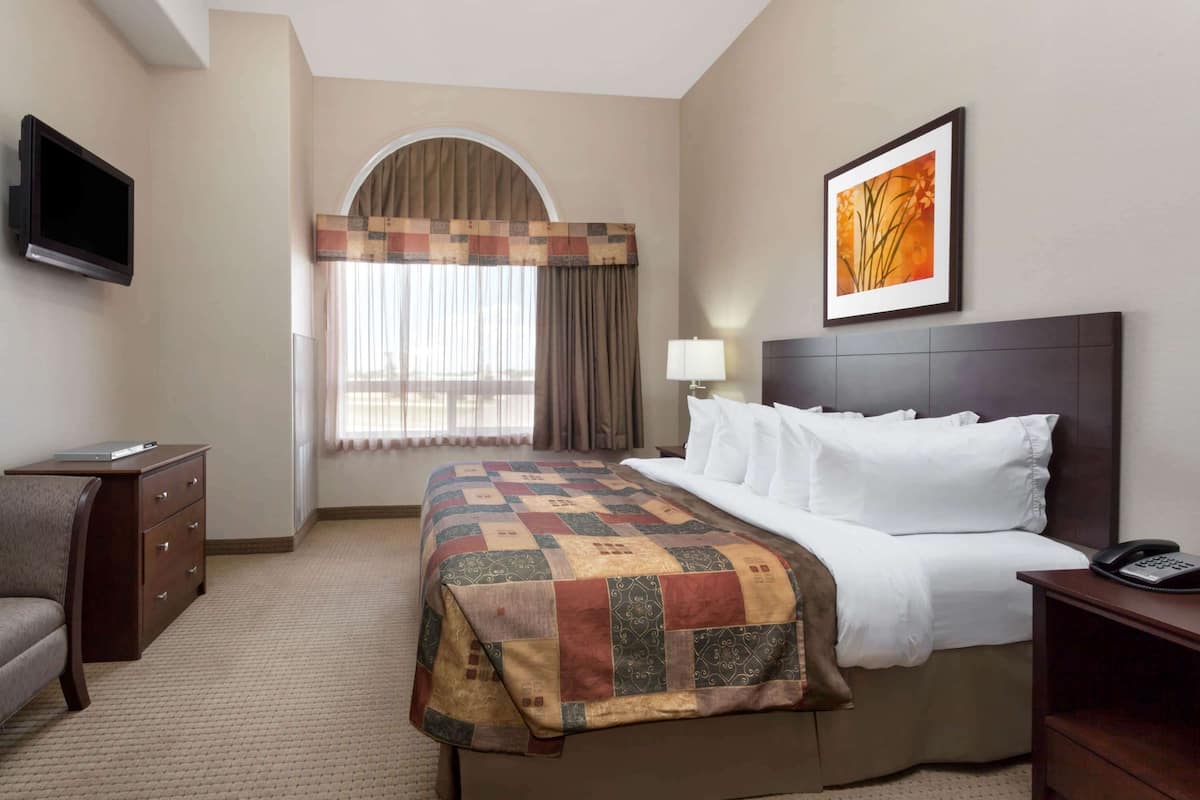 Quarto de hotel com cama, televisão, escrivaninha e janela com cortinas.