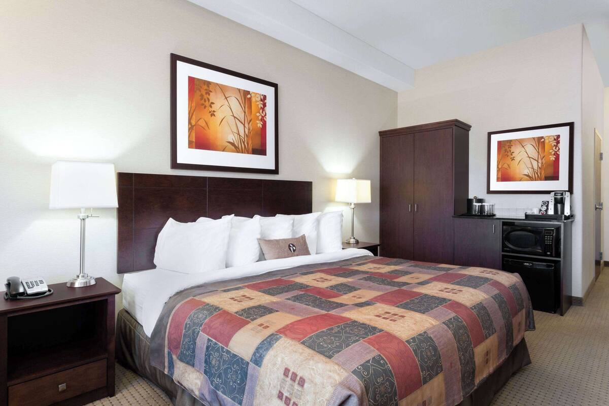 Quarto de hotel com uma cama grande, mesa de cabeceira com abajur, escrivaninha com telefone, micro-ondas e armário.
