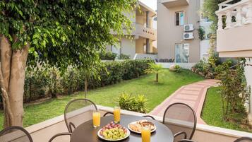 Uma área de estar externa com mesa, cadeiras e uma tábua de frutas com uvas e um copo de suco de laranja.