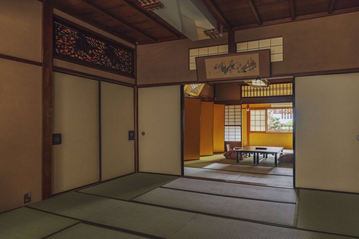 Um quarto japonês tradicional, com piso de tatame, portas deslizantes e vista para uma área de refeições.