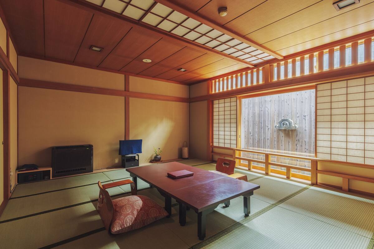 Um quarto japonês tradicional com tatames, uma mesa baixa, um assento e uma porta deslizante com vista.