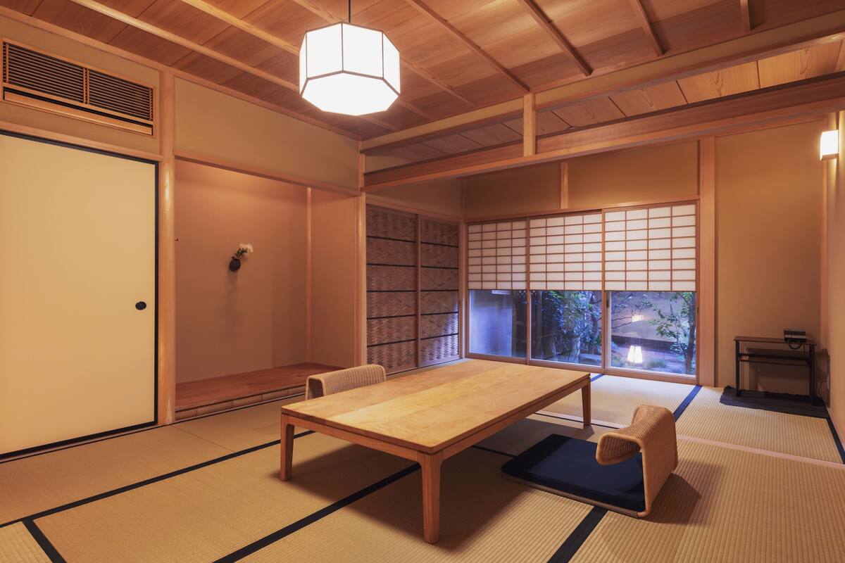 Um quarto japonês tradicional com tatames, uma mesa baixa, uma cadeira, uma porta deslizante e vista através de um shoji.