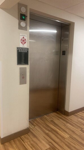 Um elevador com visor digital indicando o número 4, instruções de emergência e sinal de saída de incêndio.